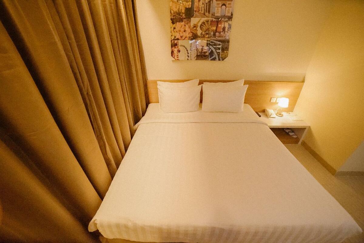 Quarto de hotel com cama, cortinas, mesa de cabeceira e luminária na parede.