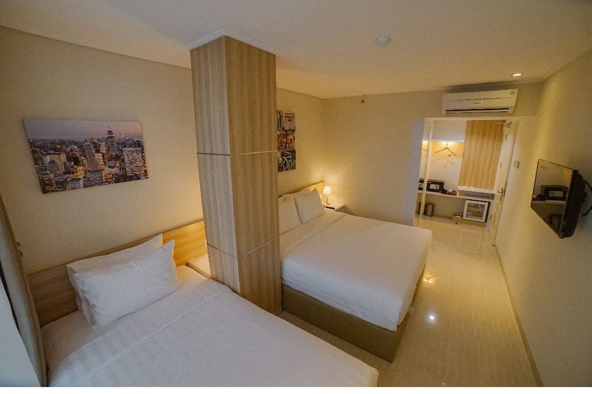 Quarto de hotel com duas camas, uma pintura de paisagem urbana, aparelho de ar condicionado e um espelho refletindo o quarto.