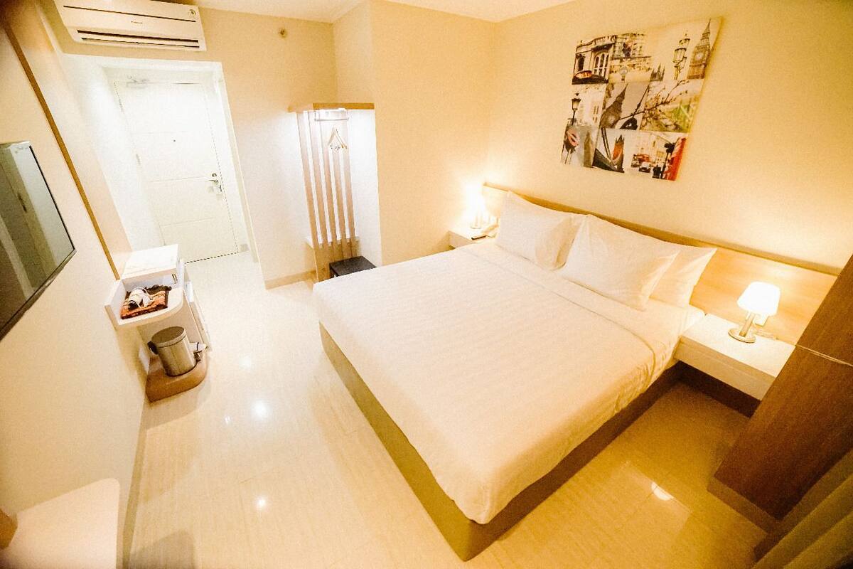 Quarto de hotel com cama grande, mesas de cabeceira, guarda-roupa, espelho e parede com quadros.