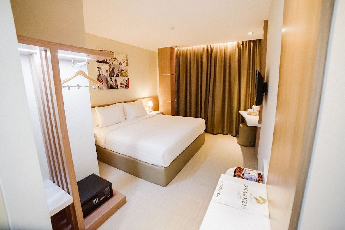 Quarto de hotel com uma cama, mesa de cabeceira, luminária, televisão e guarda-roupa.