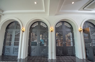 Um corredor com três portas de madeira escura e detalhes ornamentados, além de luminárias acima.