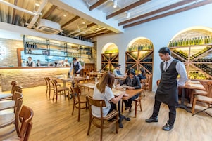 Um restaurante com mesas e cadeiras de madeira, área de bar e estantes para vinho.