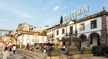 Uma praça pública com mesas ao ar livre e um edifício de destaque com a sinalização 'SANDEMAN'.