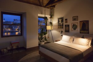 Quarto com uma janela grande, uma cama, uma mesa de cabeceira, uma luminária e diversas decorações nas paredes.