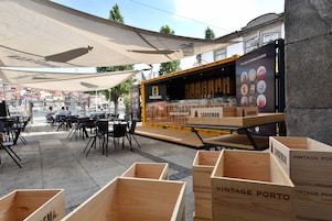 Uma área de bar ao ar livre com mesas e cadeiras, um grande anúncio da Sandeman e caixas de madeira identificadas como 'Vintage Porto'.