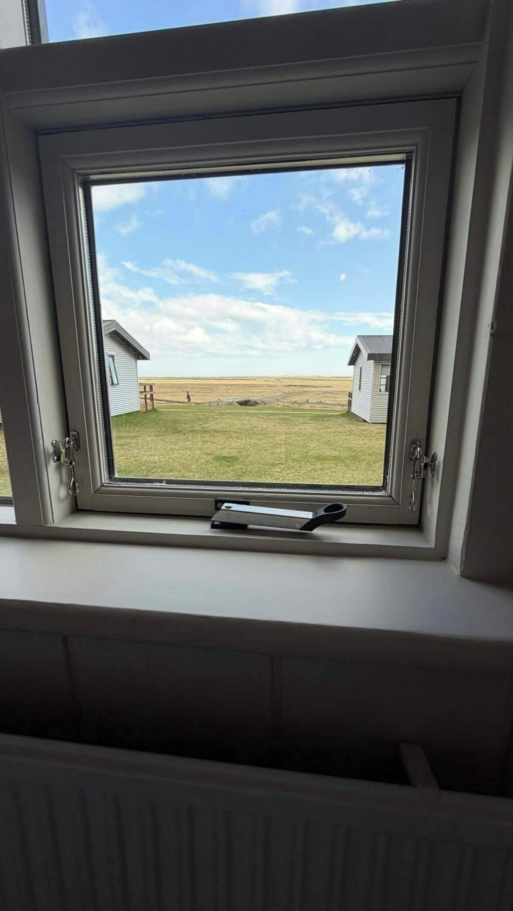 Uma janela com vista para um campo gramado e dois edifícios.