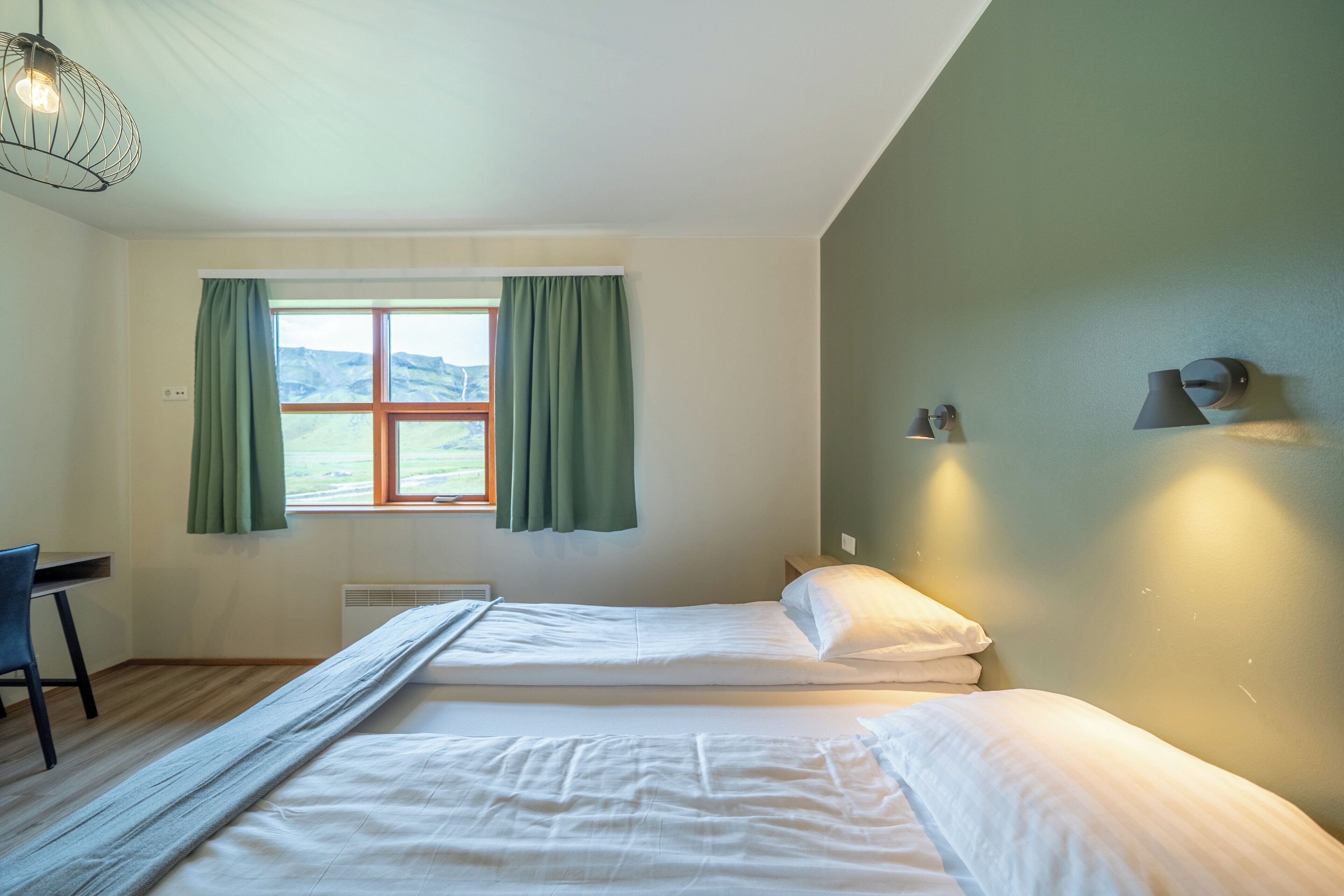 Quarto com duas camas, uma escrivaninha e janela com cortinas.