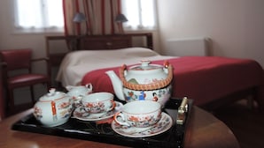 Um quarto com cama, mesa de cabeceira com bandeja e chá, e janela com cortinas.