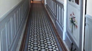 Um corredor com piso estampado, um lustre e uma porta decorada com obras de arte.
