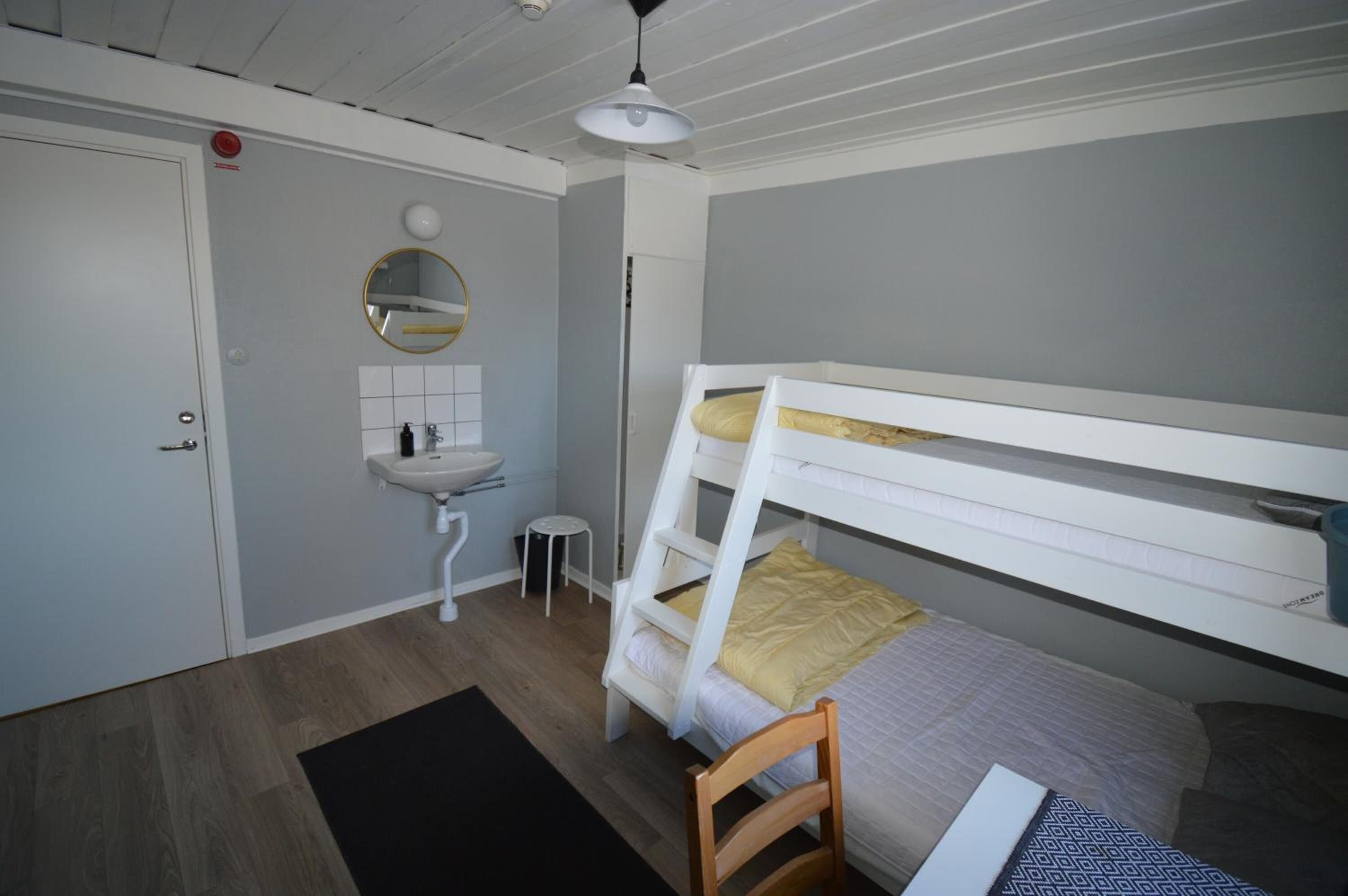 Quarto com uma cama beliche, pia, espelho e um pequeno banquinho.