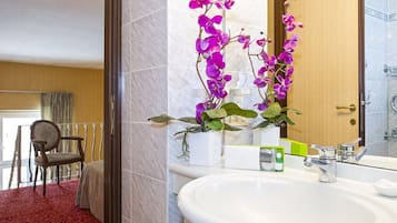 Casa de banho de hotel com uma banheira grande, um espelho e orquídeas roxas.