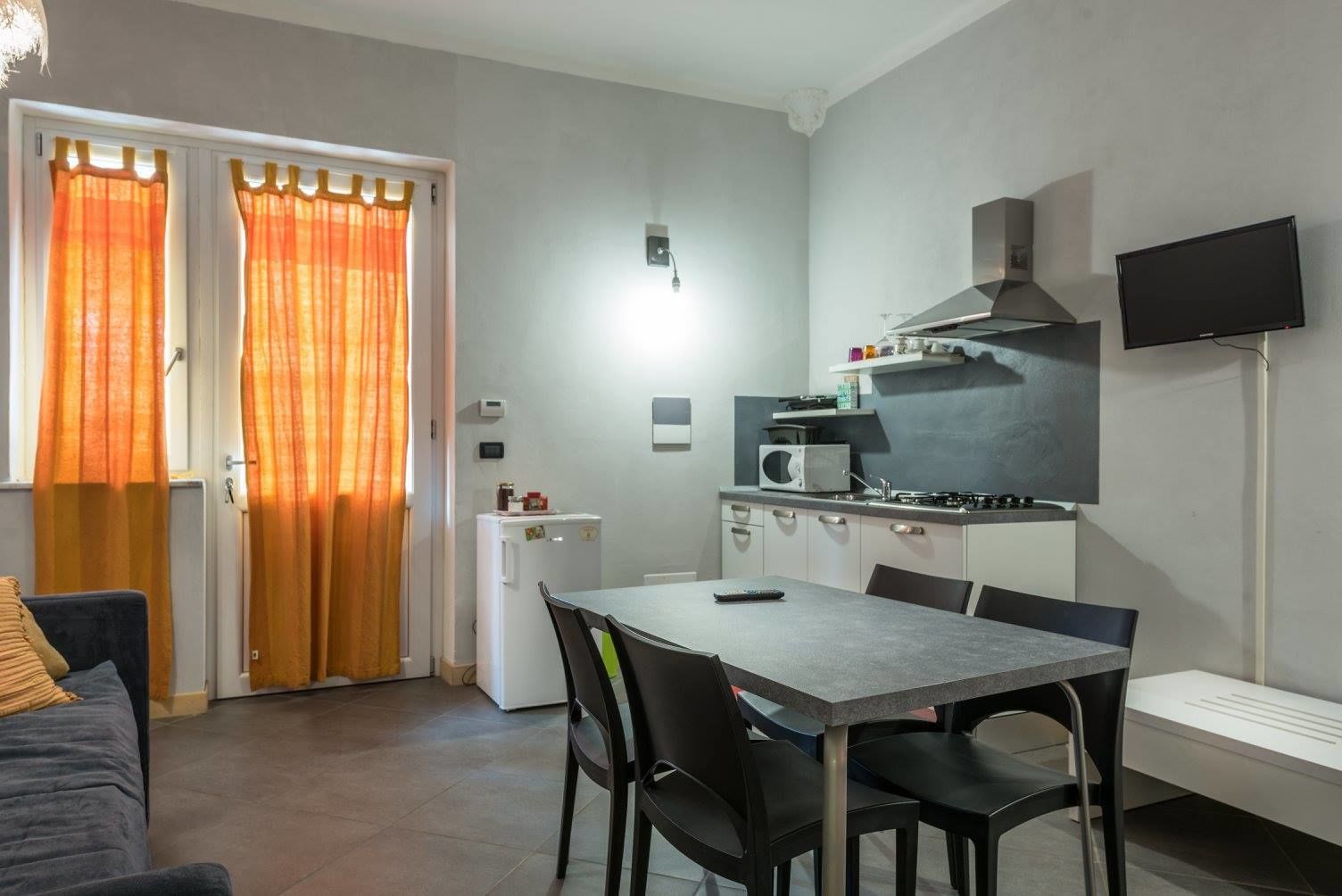 Uma cozinha compacta com mesa, cadeiras, geladeira, micro-ondas e televisão fixada na parede.