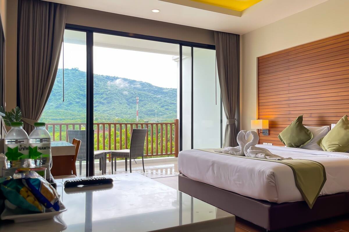 Quarto de hotel com uma cama, uma mesa com controle remoto e vista para uma paisagem montanhosa.