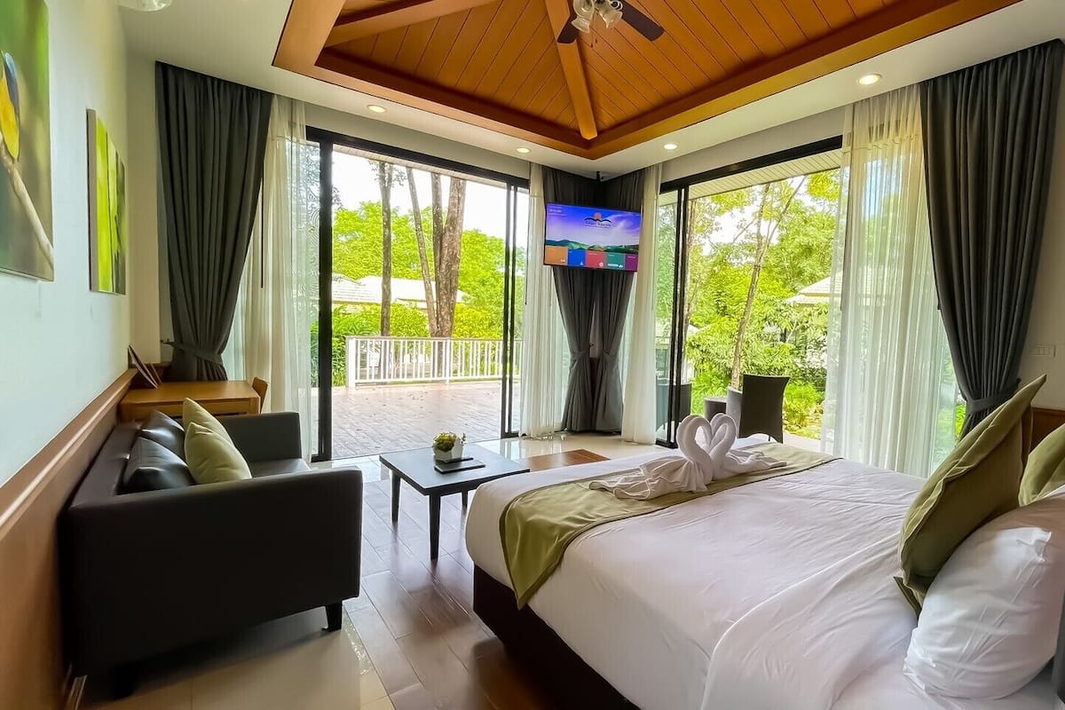 Quarto de hotel moderno com uma cama grande, um sofá, uma mesinha e uma televisão.