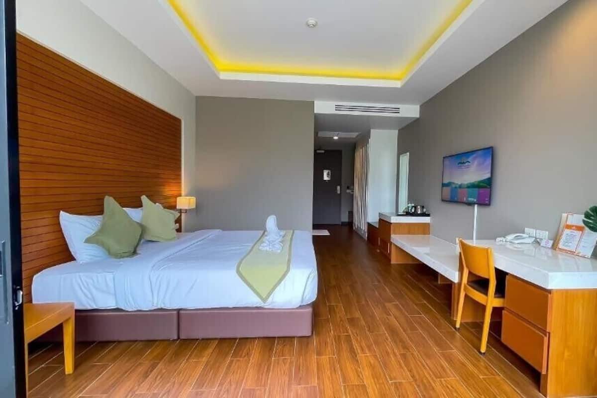 Quarto de hotel moderno com cabeceira de madeira, cama com almofadas, escrivaninha com cadeira e televisão na parede.