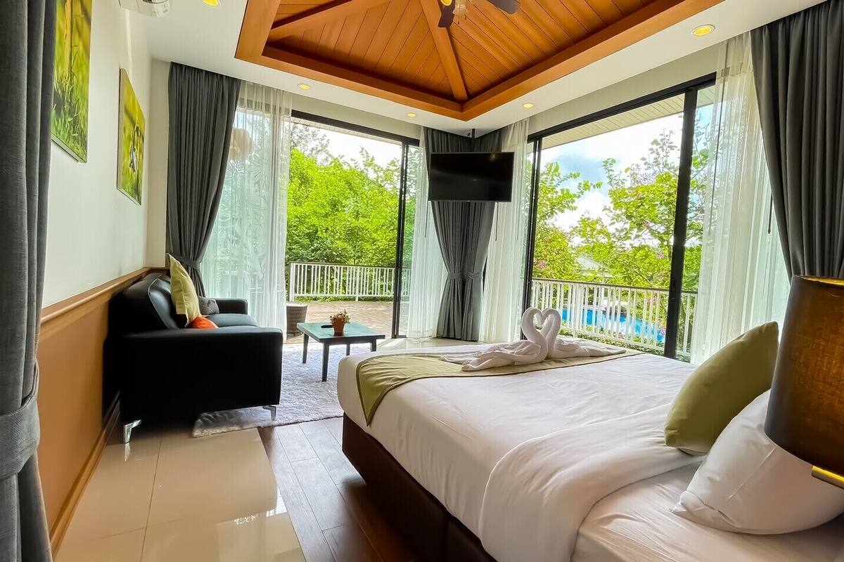 Quarto de hotel moderno com uma cama grande, um sofá, uma mesa pequena e uma varanda vista para piscina.