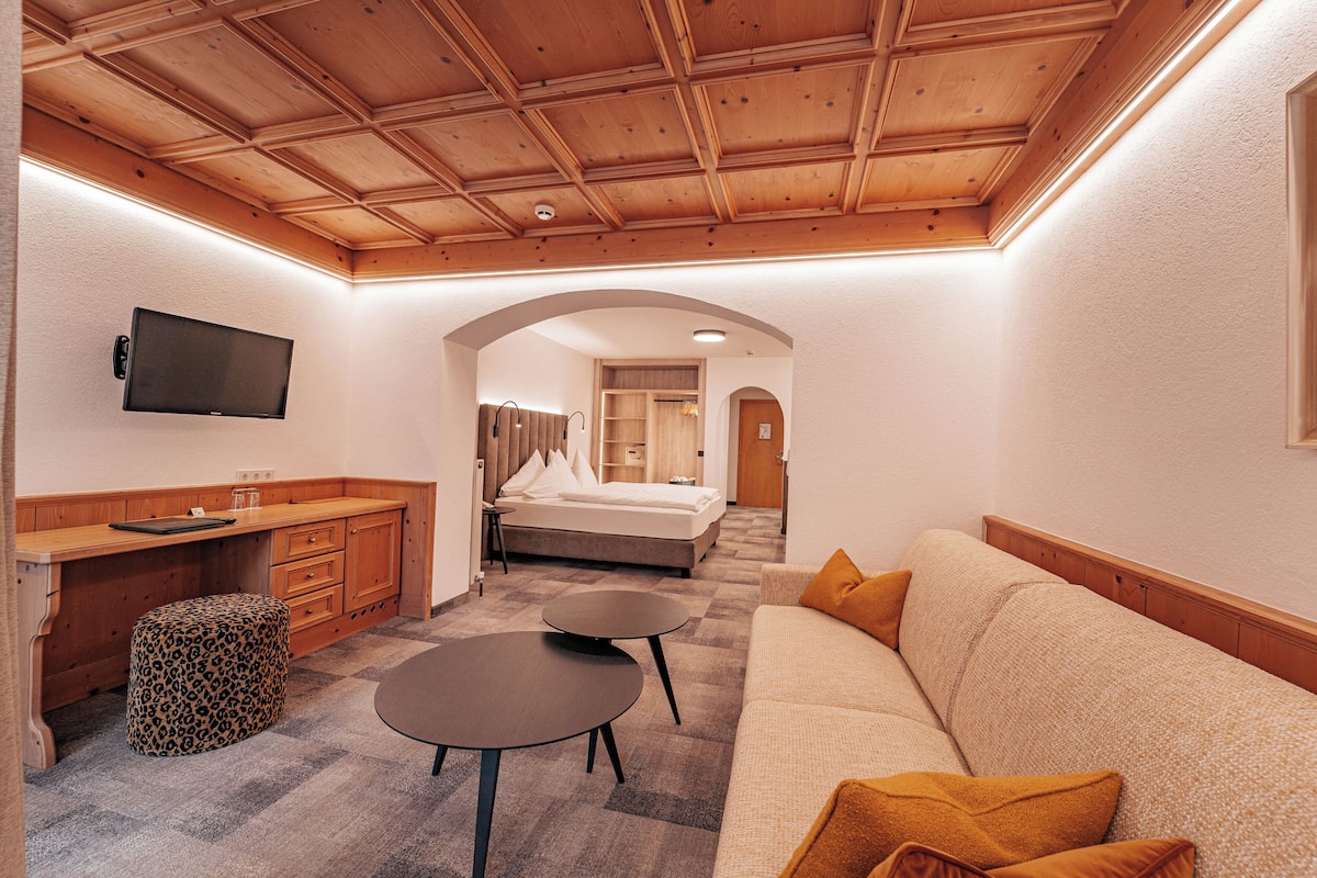 Quarto de hotel moderno com teto de madeira, TV de tela plana, sofá, cama e escrivaninha com gavetas.