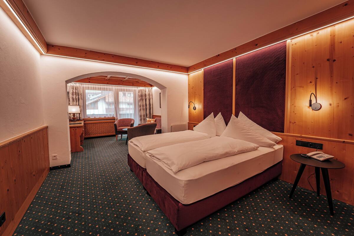 Quarto de hotel com uma cama grande, uma mesa com cadeira e uma mesinha com telefone.
