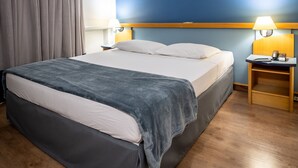 Quarto de hotel com uma cama, duas mesas de cabeceira, uma luminária e uma cortina.