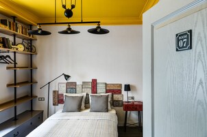 Um quarto com uma cama, uma estante de livros, uma escrivaninha e um relógio de parede.