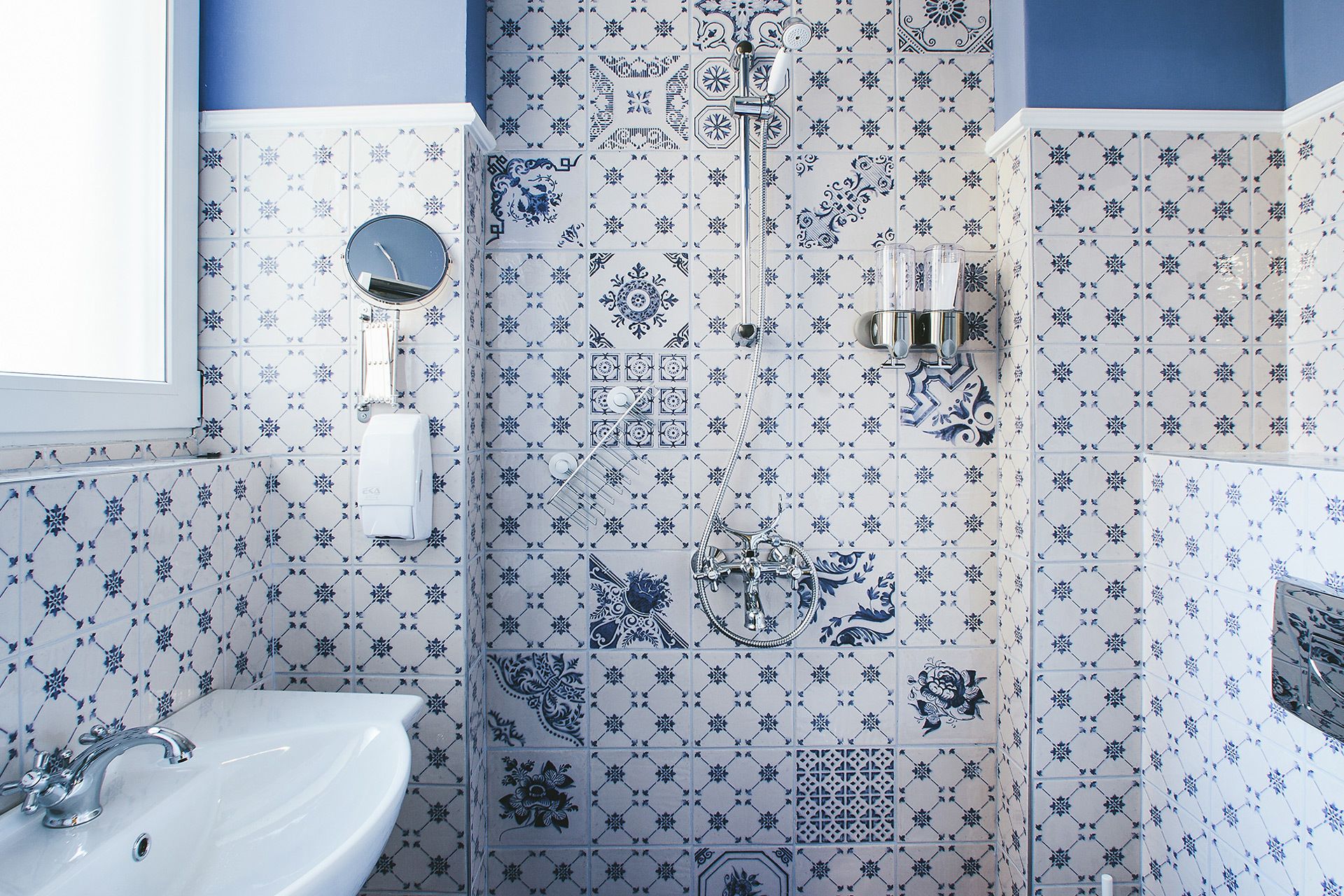 Um banheiro com azulejos azuis e brancos estampados, uma pia branca e área de chuveiro.