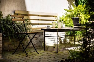 Um pátio com um banco de madeira, uma mesa e plantas em vasos.