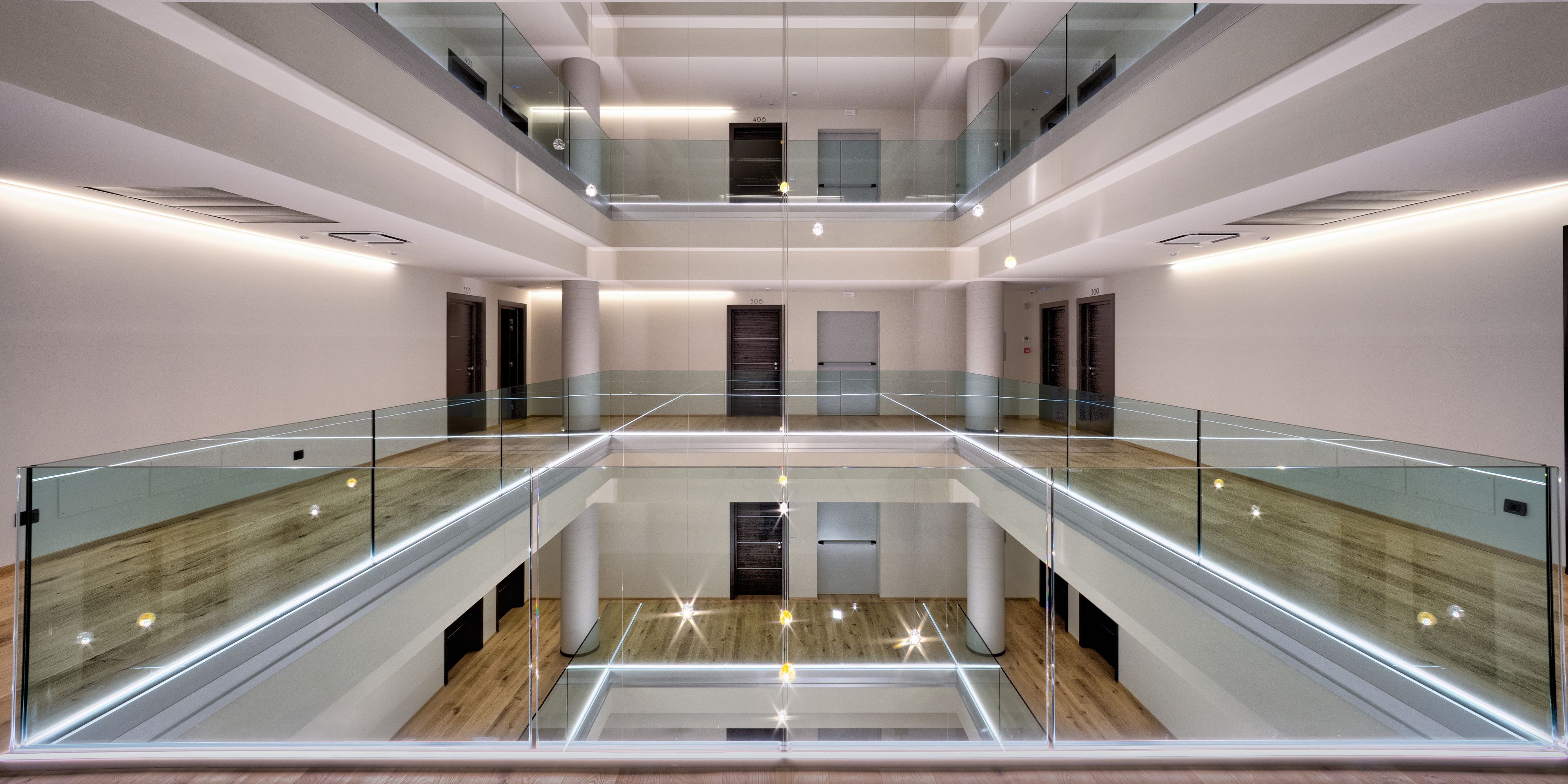 Interior com vários níveis, corrimãos de vidro, piso de madeira e iluminação moderna.