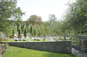 Um jardim ajardinado com muro de pedra, caminhos e sebes bem aparadas.
