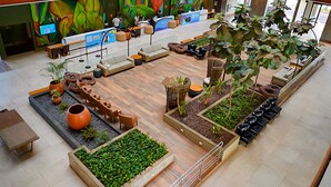 Um hall espaçoso com área de estar central, vários vasos com plantas e uma grande tela de televisão.