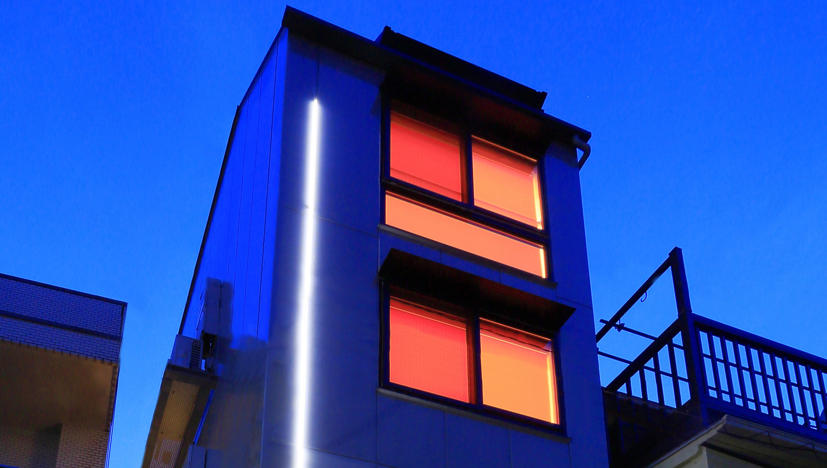 Um edifício moderno com duas janelas iluminadas e uma varanda.