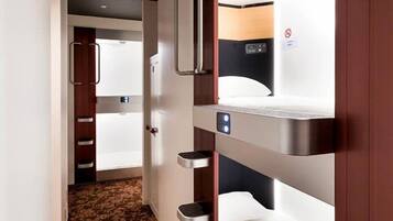 Quarto de hotel com beliches, painel de controle e porta que dá para outro quarto.