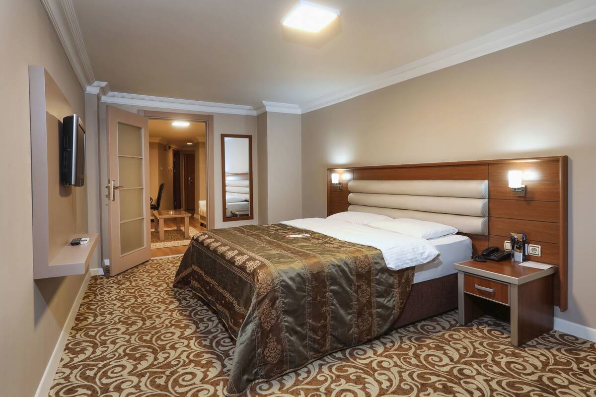 Quarto de hotel com uma cama grande, mesa de cabeceira e televisão na parede.