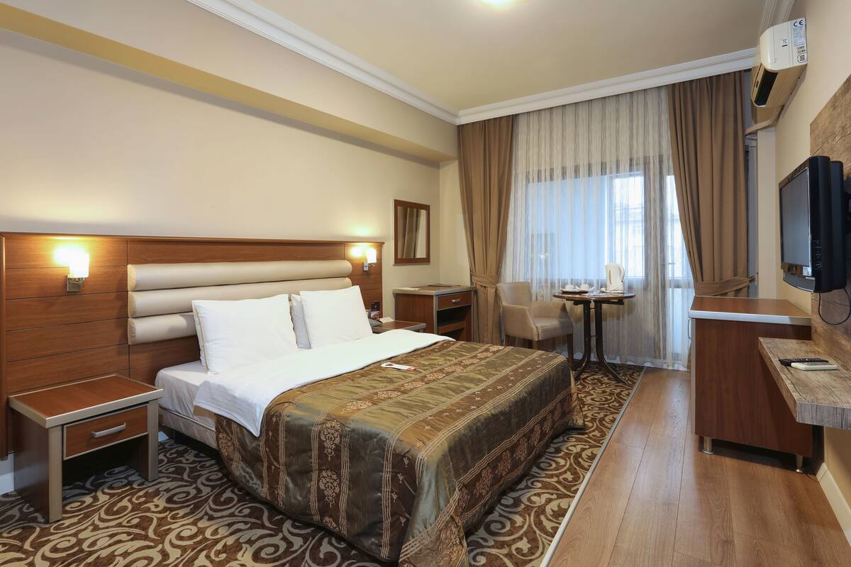 Quarto de hotel com uma cama grande, uma escrivaninha, uma cadeira e uma televisão.