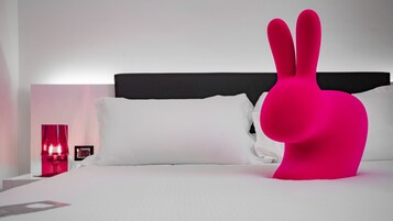 Uma cama com lençóis brancos, cabeceira preta e um objeto rosa grande que se assemelha a um coelho.