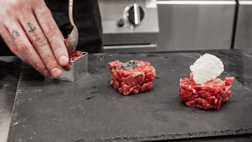Uma pessoa preparando comida em uma tábua de corte preta, em uma cozinha.