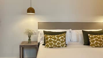 Uma cama bem arrumada com cabeceira, uma mesinha de cabeceira com um vaso de flores e uma luminária pendente.
