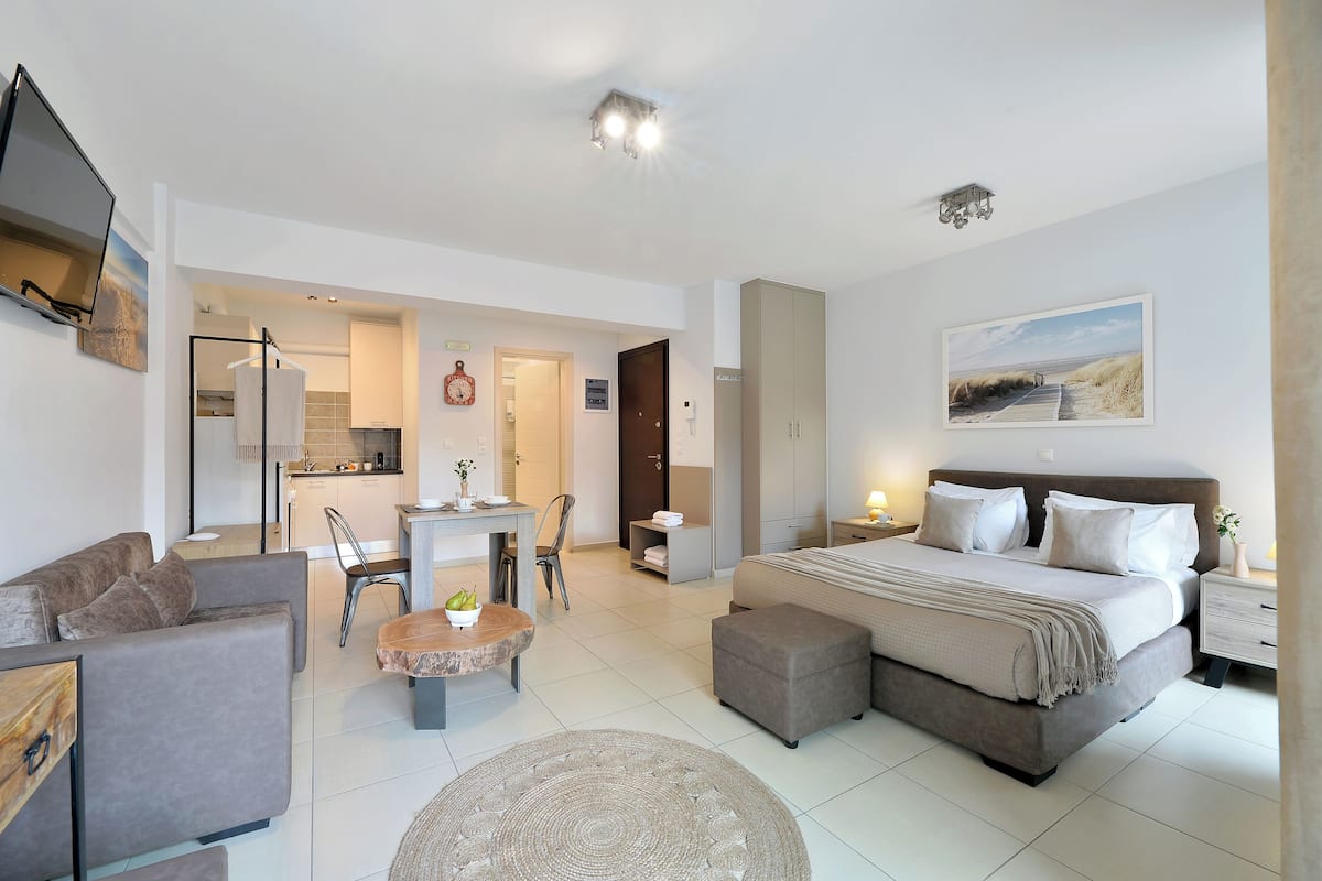 Quarto moderno com uma cama grande, um sofá, uma mesa de jantar e uma área de cozinha ao fundo.