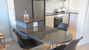 Uma cozinha moderna com uma mesa de jantar de vidro, cadeiras pretas e eletrodomésticos de aço inoxidável.