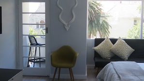 Quarto com cama, sofá com almofadas estampadas, cadeira e objeto decorativo fixado na parede.
