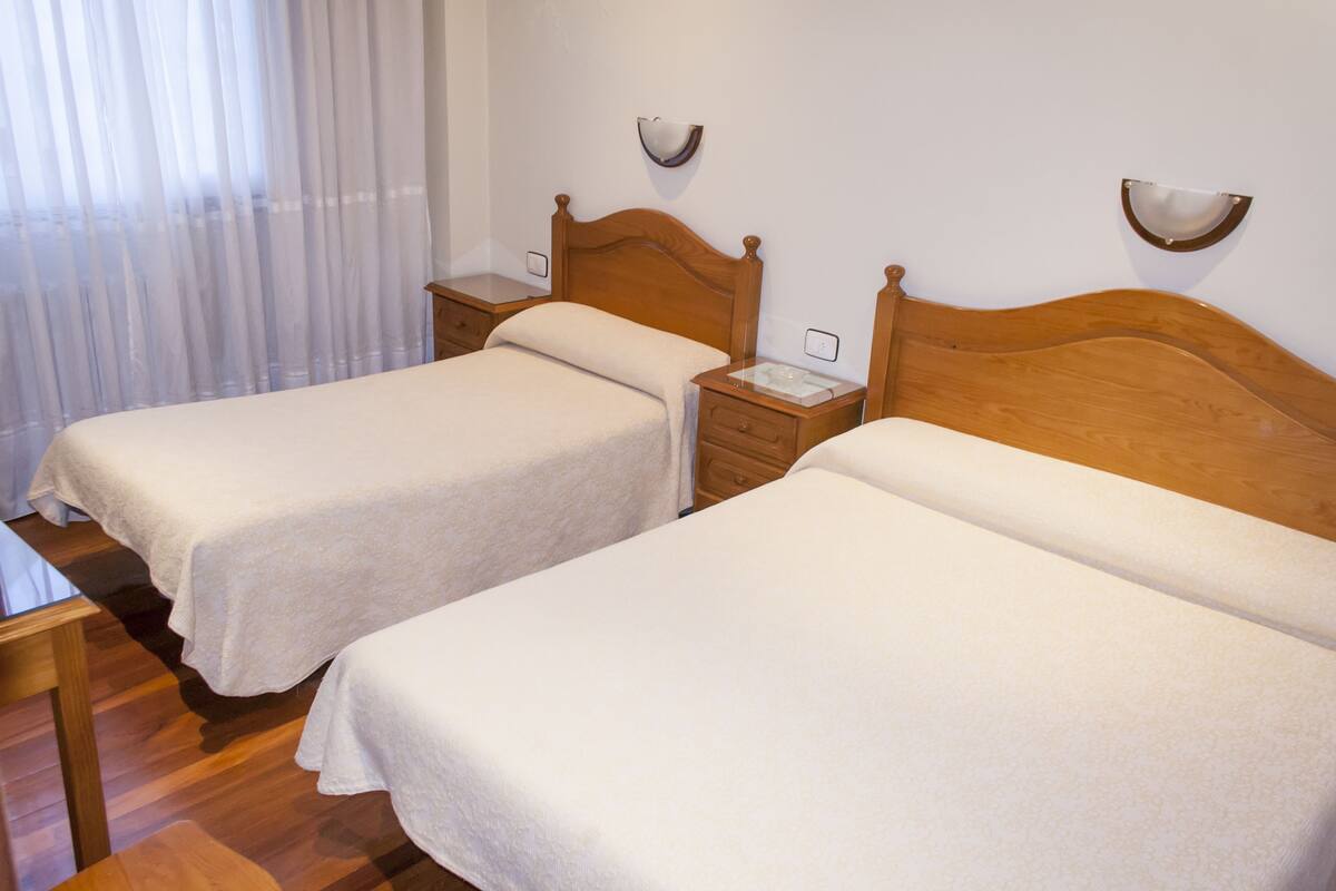 Quarto de hotel com duas camas de solteiro, cabeceiras de madeira, mesas de cabeceira e uma pequena mesa.