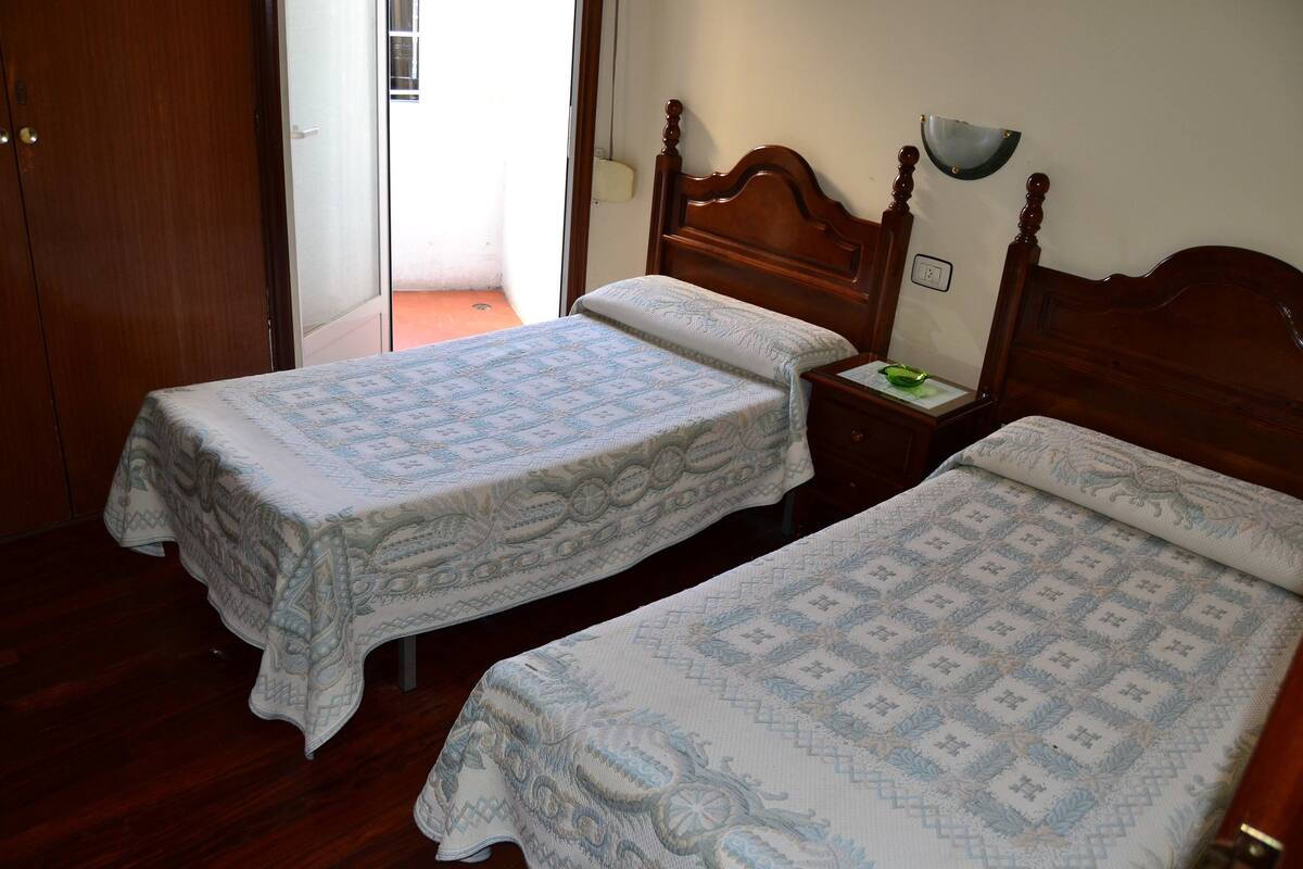 Quarto com duas camas de solteiro, cabeceiras de madeira, mesa de cabeceira com abajur e guarda-roupa.