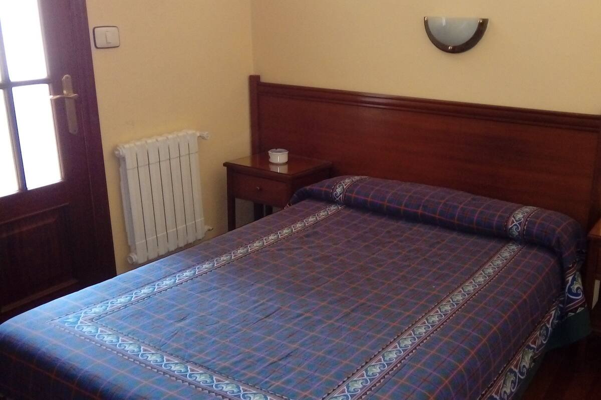 Quarto com cabeceira de madeira, mesa de cabeceira com luminária e radiador.