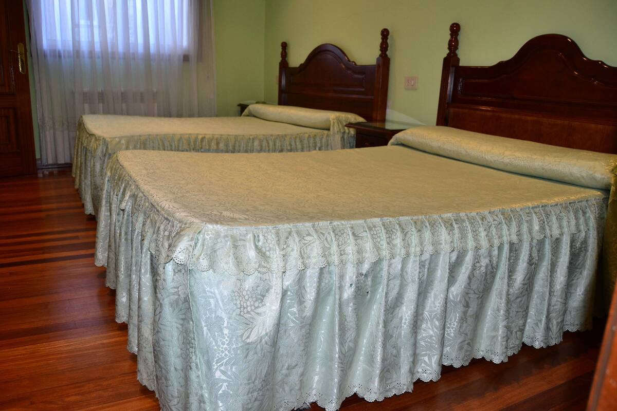 Quarto com duas camas de madeira, com cabeceiras e peseiras combinando, cobertas por colchas rendadas.