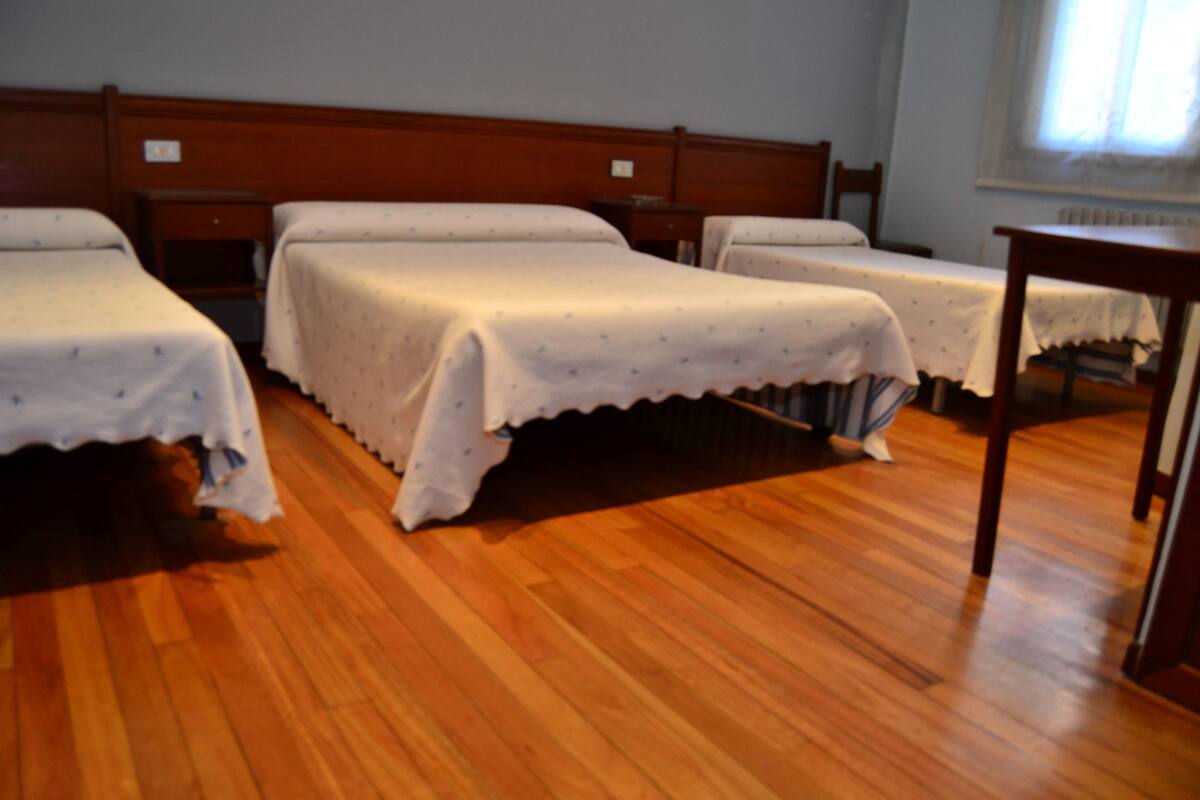 Quarto com três camas de solteiro, piso de madeira e uma pequena mesa.