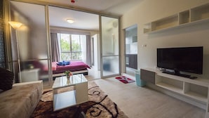 Uma sala de estar moderna com sofá, mesa de centro, televisão e portas de vidro deslizantes que dão para uma varanda.