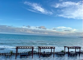 Um pátio à beira-mar com pérgulas de madeira e mesas com vista para o oceano.