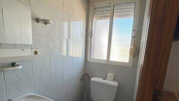 Uma casa de banho pequena com uma sanita, lavatório e janela brancos.