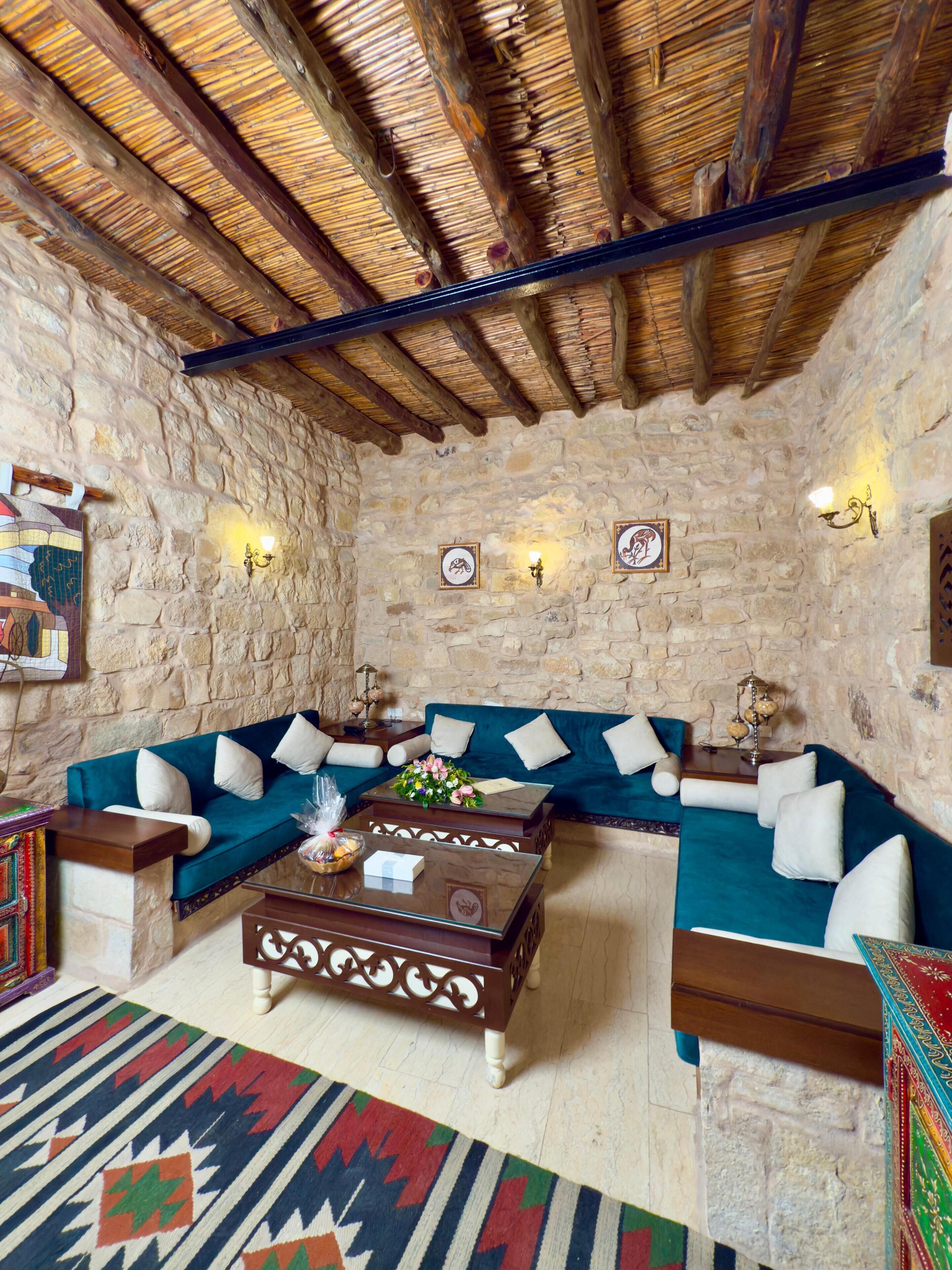 Um quarto acolhedor com parede de pedra, teto de madeira, sofá azul e mesa de centro, além de um tapete estampado.