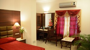 Quarto de hotel com cama, escrivaninha, cadeira, mesa, luminária e planta em vaso.