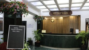 Área de recepção de hotel com balcão, relógio e placa indicando o nome e a data do hotel.